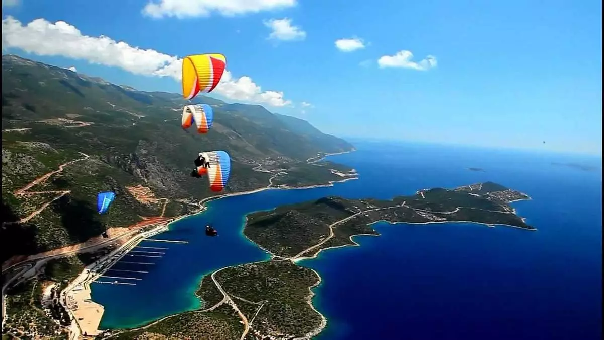 A group of paragliders travel over the sea.